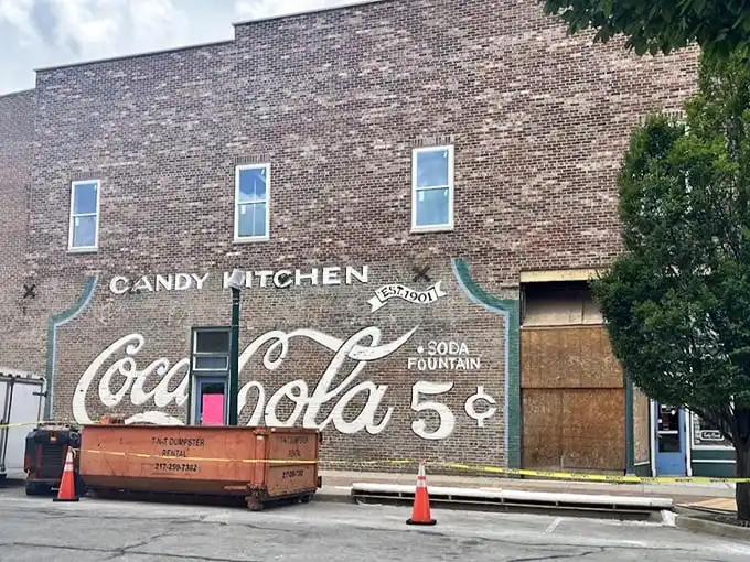 The historic brick façade of Flesor's Candy Kitchen stands as a time capsule in downtown Tuscola, complete with vintage Coca-Cola signage promising sweet nostalgia inside.