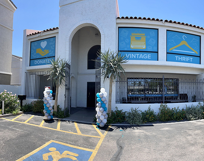 The pristine white exterior of Thrift to Thrive welcomes bargain hunters with its Mediterranean-inspired architecture and cheerful blue window displays.