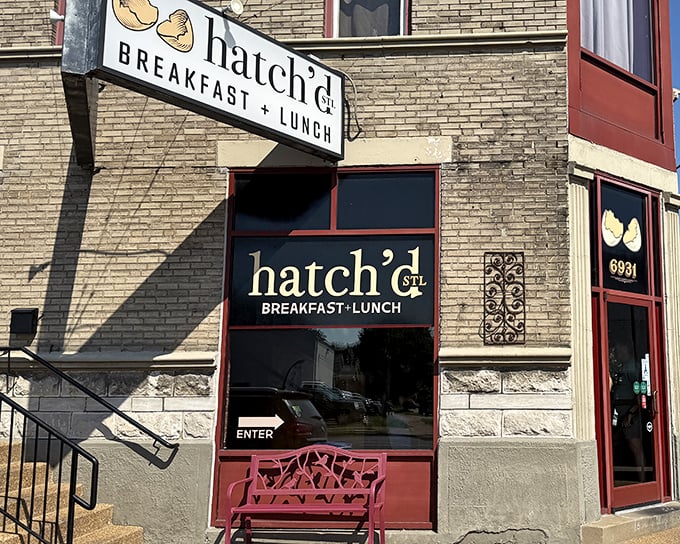 The iconic Hatch'd STL storefront beckons with its charming red bench and cracked egg logo—like a breakfast beacon in St. Louis brick.
