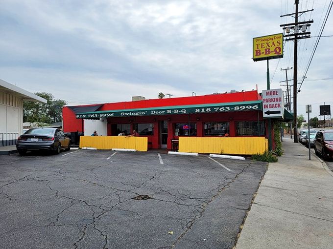 The bright red exterior of Swinging Door BBQ stands out like a beacon of hope for hungry travelers. Those wagon wheels aren't just for show—they're rolling you toward flavor town.