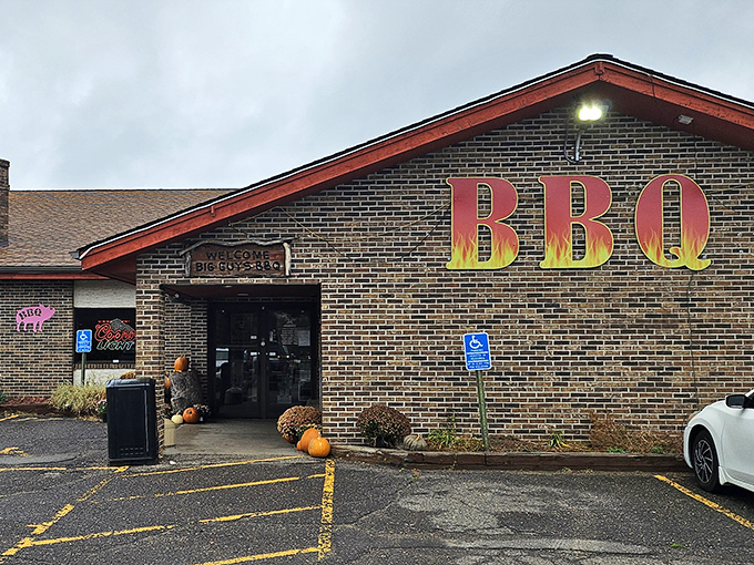 The brick facade of Big Guy's BBQ Roadhouse stands like a temple to smoked meat, its fiery BBQ sign a beacon to hungry travelers on Wisconsin highways.