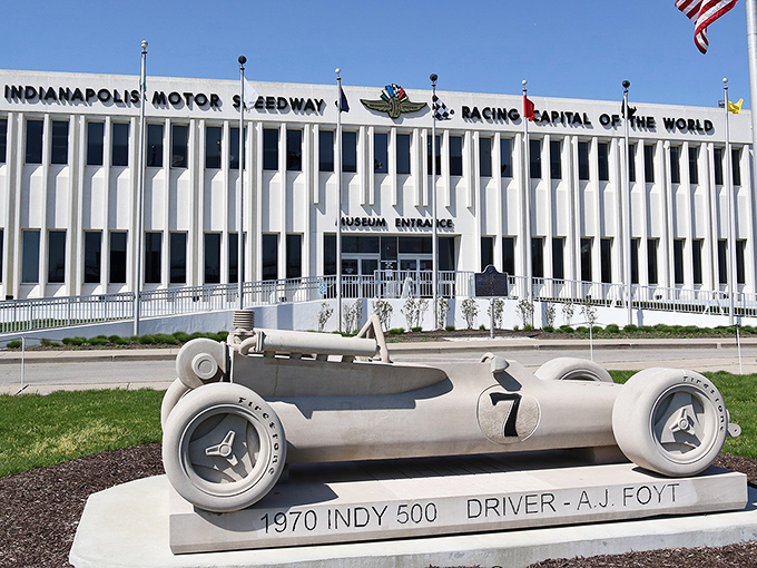The modernist façade of the Indianapolis Motor Speedway Museum stands proudly as the guardian of racing history, with A.J. Foyt's 1970 winner immortalized in concrete out front.