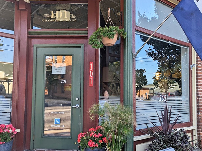 The charming exterior of Kitchen 101 beckons with its green door and vibrant flowers, like a culinary oasis on Chambersburg Street.