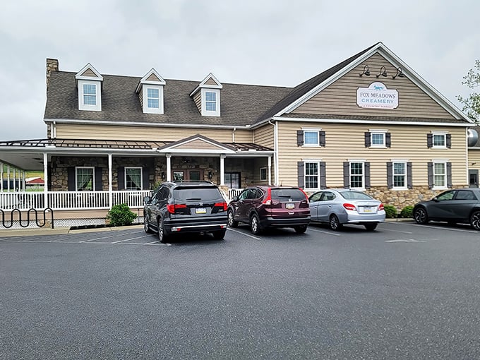 The farmhouse-style exterior of Fox Meadows Creamery welcomes visitors with its stone facade and inviting wraparound porch—architectural proof that calories consumed on rocking chairs don't count.