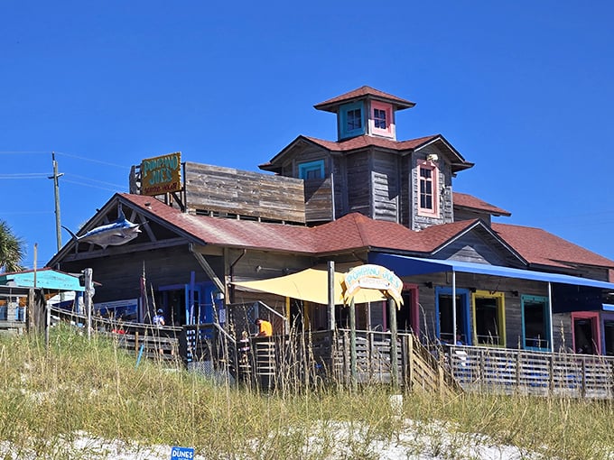 Pompano Joe's weathered wooden exterior isn't trying to impress anyone—yet somehow manages to charm everyone with its colorful Caribbean-inspired architecture perched right on the dunes.
