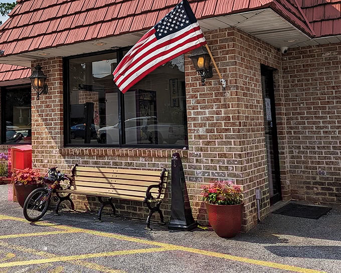 Classic Americana at its finest – a brick exterior with a welcoming bench, vibrant flower pots, and that iconic red roof that practically whispers "come hungry, leave happy."