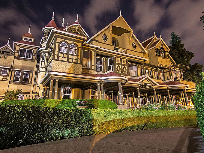 The Winchester Mystery House glows with eerie elegance at night, its Victorian façade hiding architectural oddities that would make M.C. Escher scratch his head in confusion.