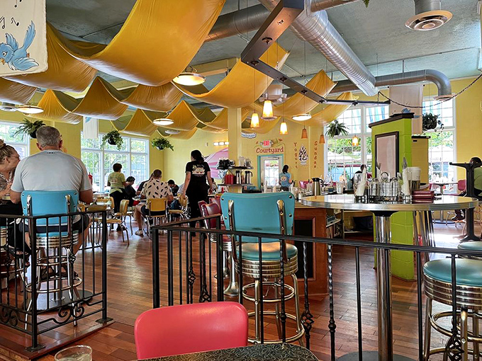 The bustling interior where breakfast magic happens. Yellow fabric ceiling, hanging plants, and happy diners – a morning trifecta.