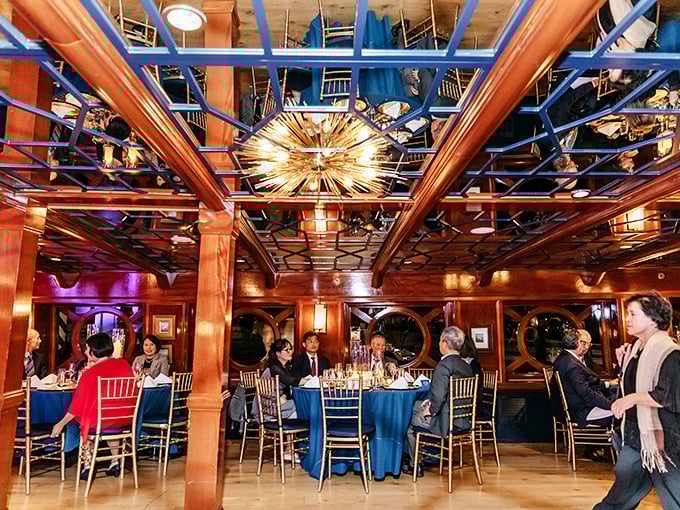 Under a starburst chandelier, diners gather like modern-day seafarers, trading stories instead of spices across tables dressed in nautical blue.