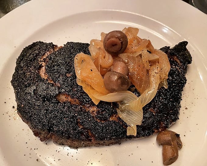This blackened steak with caramelized onions and mushrooms isn't just cooked – it's been transformed through fire and skill into something transcendent.