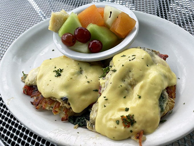 Eggs Benedict reimagined with a side of fresh fruit—proof that healthy and indulgent can coexist on the same glorious plate.