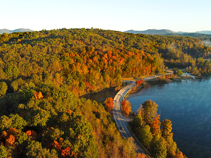 Winding roads hug the shoreline where autumn's fiery display reflects in still waters, creating nature's perfect mirror image.