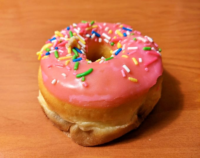 A single pink-frosted donut with rainbow sprinkles—the kind that makes grown adults smile like they're eight years old again. Simple joy, perfectly executed.