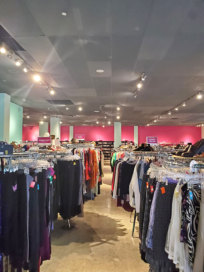 Rows of carefully organized women's clothing create a boutique experience at thrift store prices. The pink walls add a touch of retail therapy to the bargain hunt.