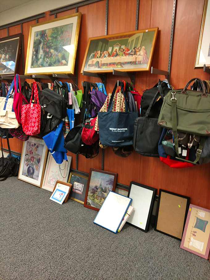 Religious art hangs above a colorful array of bags—the juxtaposition creating an unintentional gallery where the sacred and practical coexist in thrift store harmony.