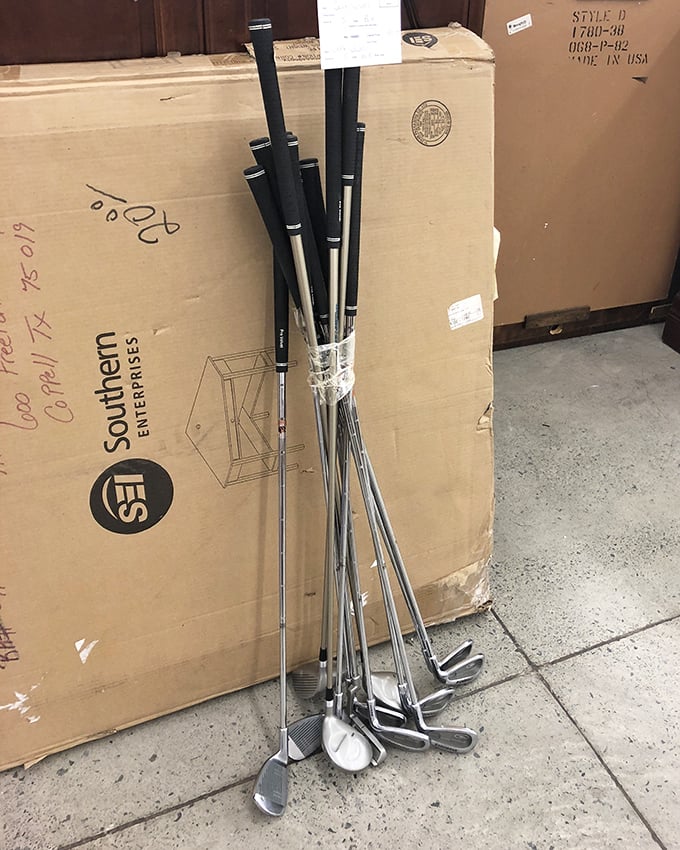 Golf clubs lean casually against cardboard, like athletes resting between games. Weekend warriors and beginners alike find sporting bargains here.