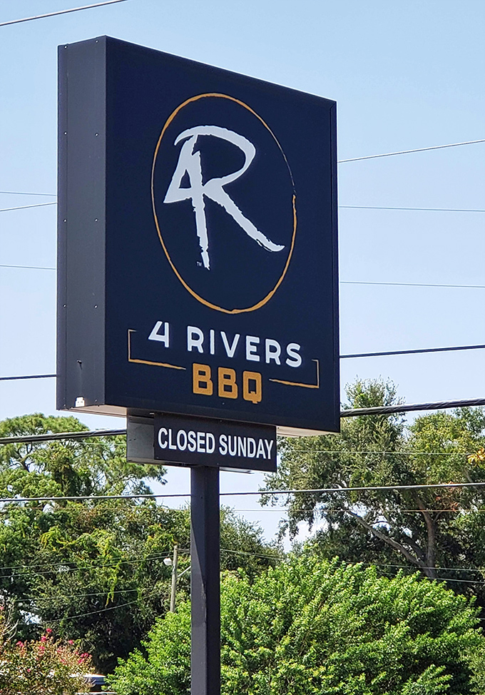 The 4 Rivers logo stands tall against the Florida sky, a beacon for BBQ pilgrims. Note the "Closed Sunday" – even pitmasters need a day of rest.