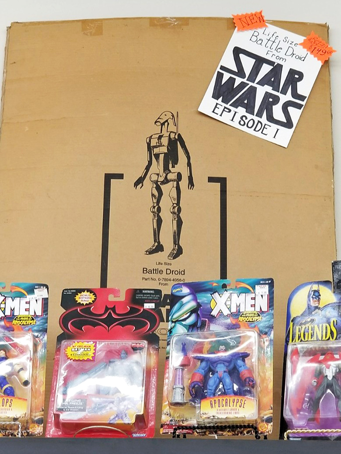 A Star Wars battle droid box surrounded by superhero figures—childhood dreams preserved in plastic, ready for new adventures.