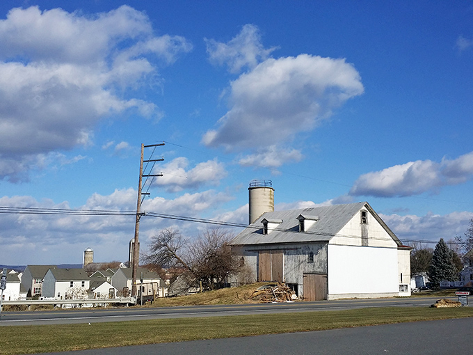 A rural farm with weathered buildings and tall silos captures Blue Ball's agricultural heritage against a cloud-dotted sky.