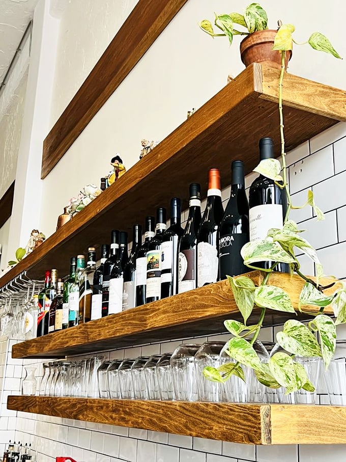 The wine shelf stands like a liquid library, each bottle a story waiting to be paired with your pizza adventure.