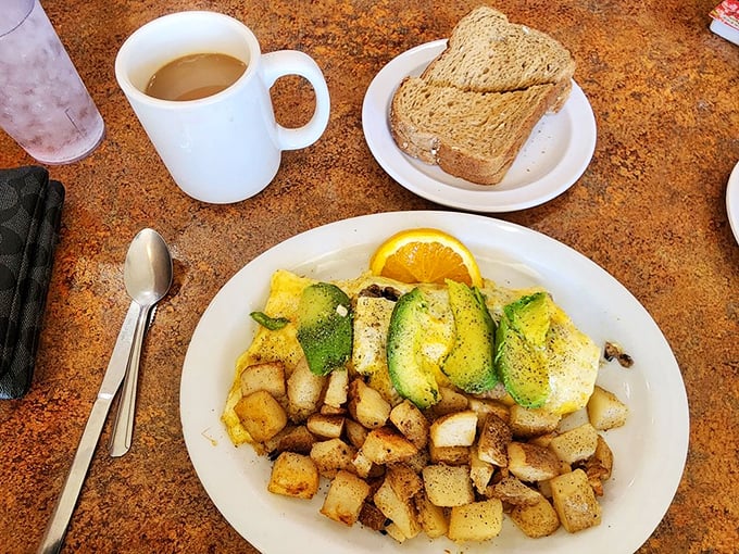 Fresh fruit and whole wheat toast play supporting roles to the real star—a vibrant omelet adorned with avocado slices like emerald medals of honor.