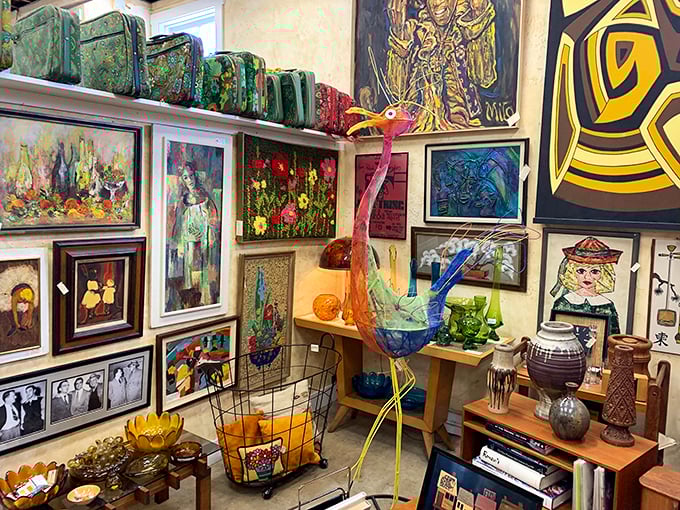 Art stacked three-deep against walls, sculptures perched like exotic birds—this booth feels like the storage room of a small eccentric museum.