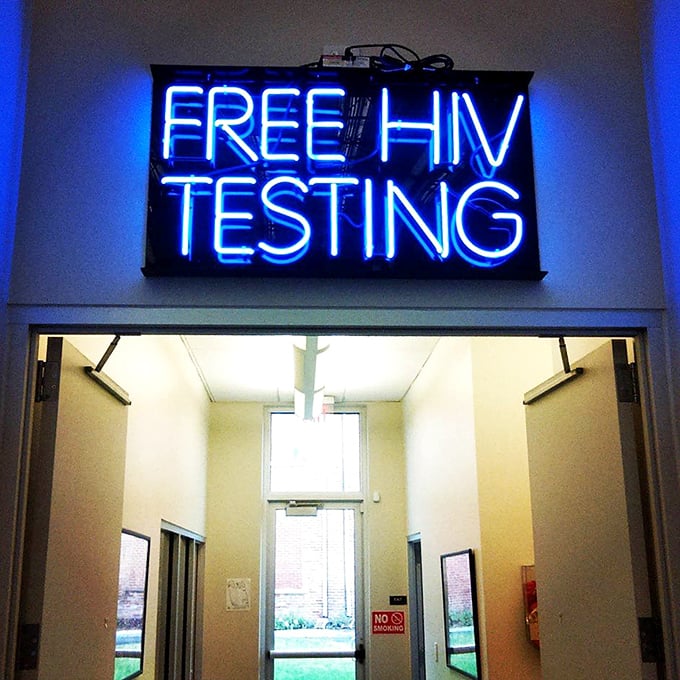 The neon "FREE HIV TESTING" sign highlights the store's mission beyond retail—providing essential health services that directly benefit from your shopping dollars.