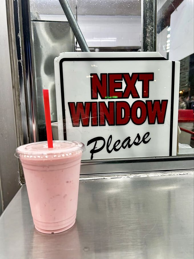 The "Next Window Please" sign paired with a strawberry shake—a pink reminder that good things come to those who follow the rules.