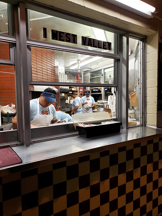 The kitchen window offers a glimpse into the organized chaos where pastrami dreams are assembled with practiced precision.