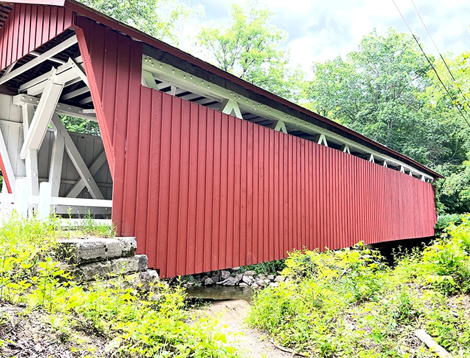 The bridge stretches across the landscape like a brushstroke of history, its vibrant red siding a bold statement against summer greens.