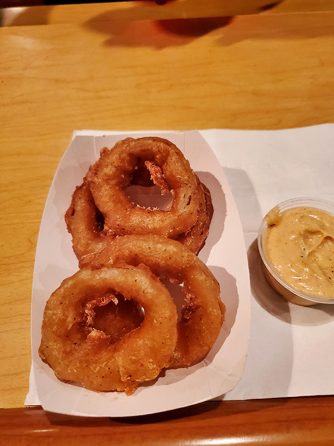 Golden onion rings with a side of dipping sauce – circular perfection that makes you wonder why squares get all the attention.