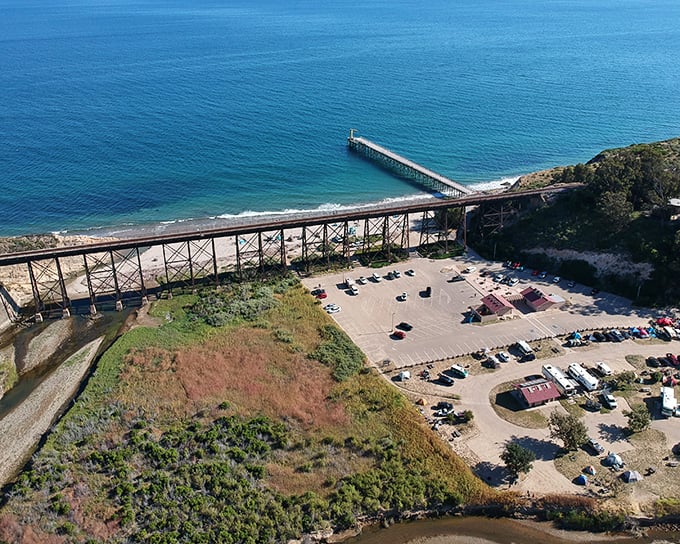 The ultimate panorama where railroad trestle meets pristine beach—proof that sometimes industrial and natural beauty can coexist like old friends.