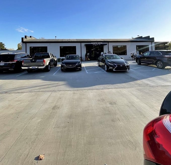 A parking lot full of cars belonging to people making excellent life decisions today. The white building promises refuge from ordinary drinking.