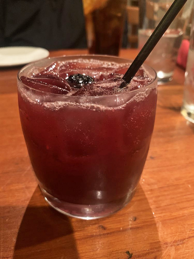 A cocktail the color of sunset, promising vacation vibes regardless of your PTO status. That blackberry isn't just garnish—it's the exclamation point on liquid relaxation.