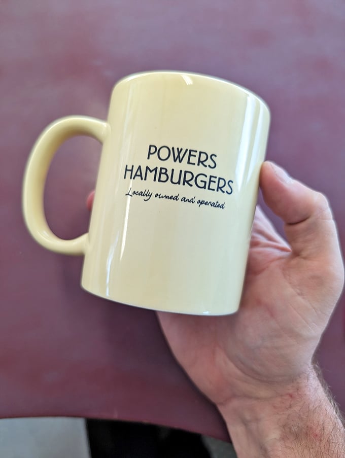 Powers' coffee mug proudly proclaims its local roots. In a world of corporate chains, this yellow ceramic vessel represents burger independence.
