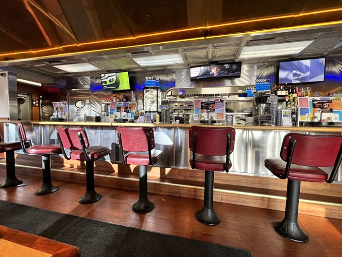 The counter seating offers front-row tickets to the culinary show—red swivel chairs and stainless steel backdrop creating that quintessential diner experience.