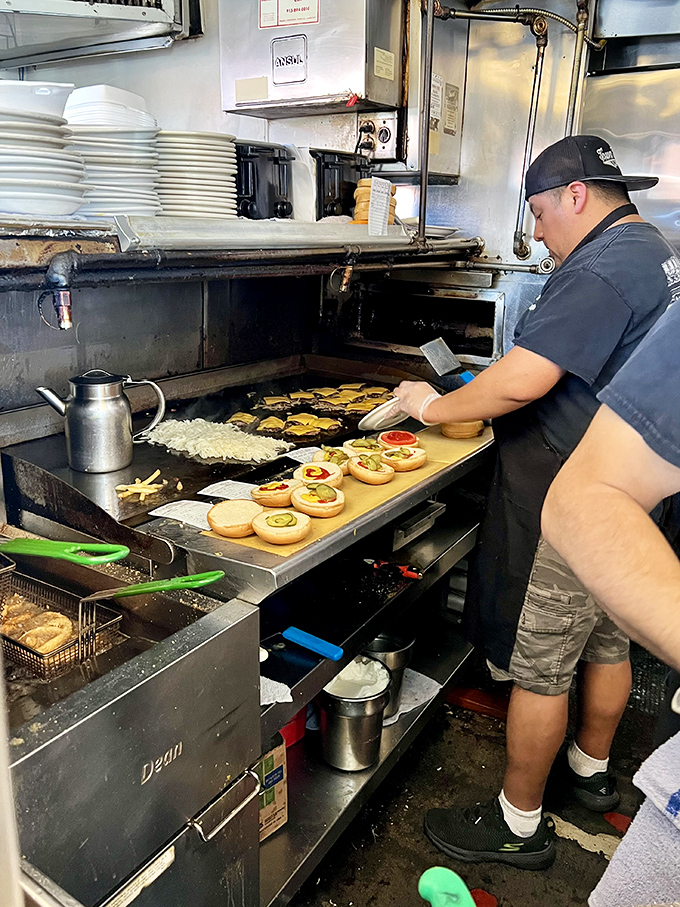 The kitchen dance – where burgers meet buns and onions sizzle into submission on a grill seasoned by decades of use.