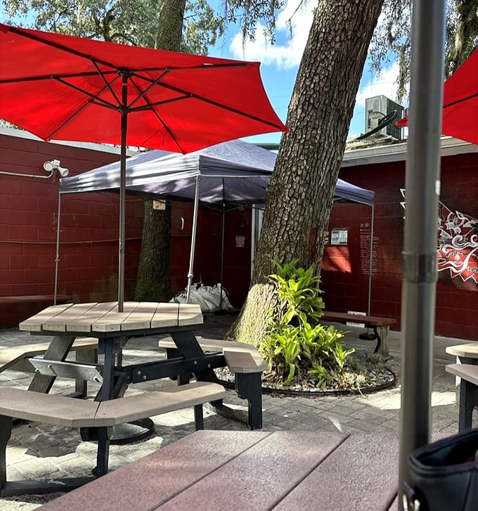 Outdoor dining under oak trees and red umbrellas – nature's perfect setting for consuming smoked meats while contemplating life's greatest pleasures.