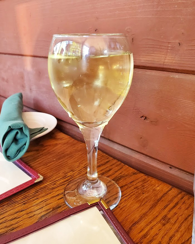 A glass of crisp white wine against rustic wood – like a little poem about the perfect marriage of refinement and comfort that defines this place.
