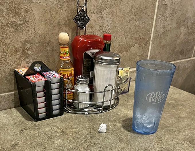 The condiment caddy—unsung hero of diner dining. That tabletop collection transforms good meals into personalized perfection.