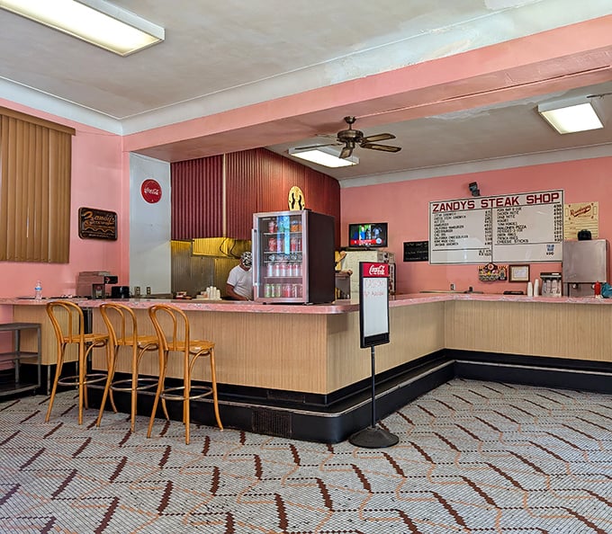 The counter where dreams come true – pink Formica, wooden stools, and the promise of a perfect cheesesteak just moments away.