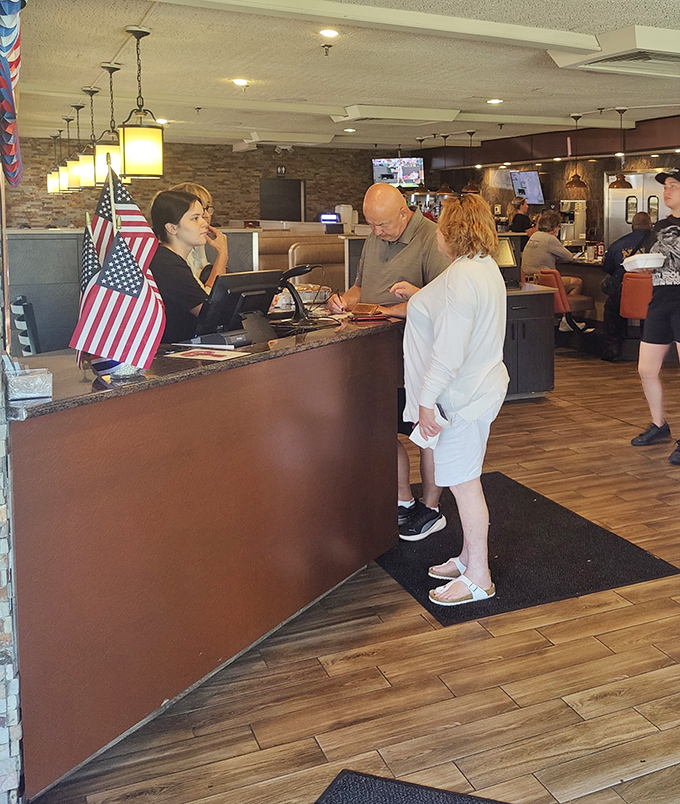The front desk—first checkpoint on your journey to comfort food nirvana, complete with American flags that remind you this is democracy in delicious action.