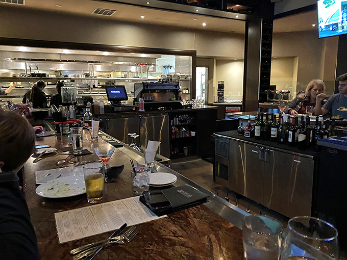 A glimpse into the kitchen reveals the orchestrated chaos where culinary magic happens—stainless steel, focused chefs, and sizzling anticipation.
