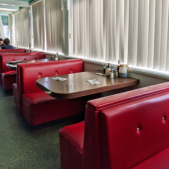 Those red vinyl booths have absorbed more stories than a librarian. Each cracked cushion is a badge of honor earned through decades of service.