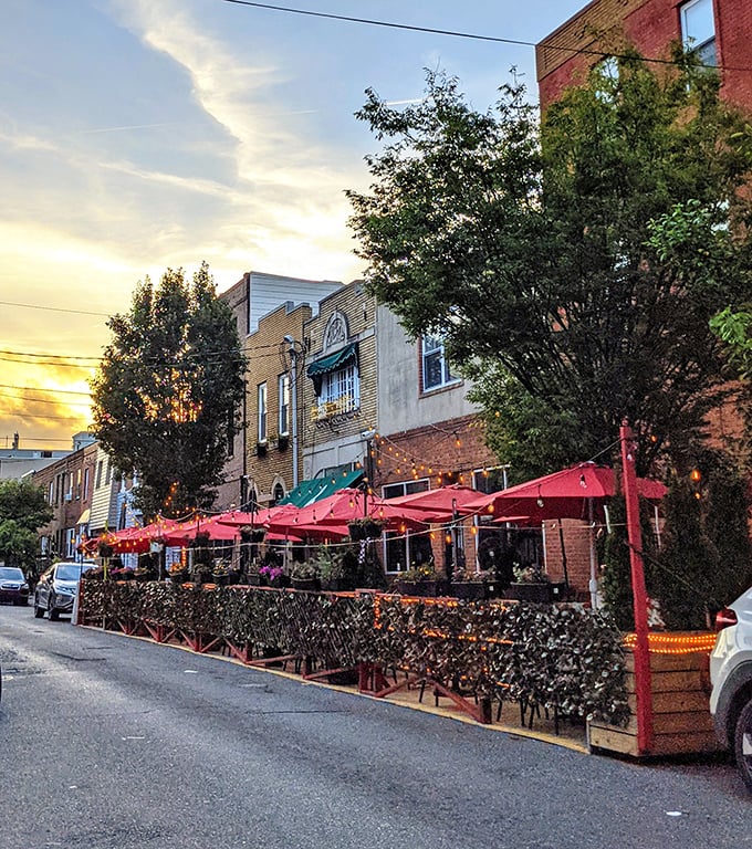 As dusk settles over South Philly, the Victor Café's outdoor dining area becomes a magical urban oasis under red umbrellas and twinkling lights.