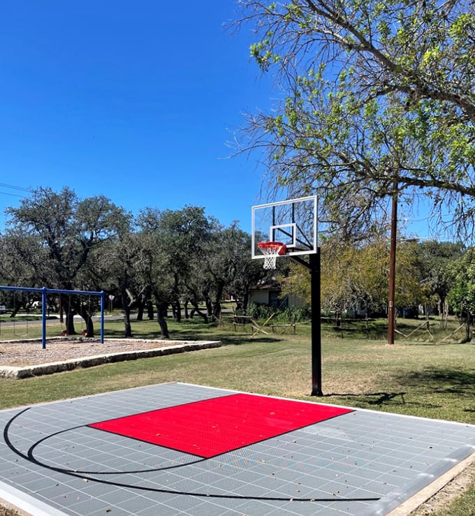 A basketball court where dreams of NBA stardom flourish under Texas skies, complete with the perfect red landing zone for spectacular moves.