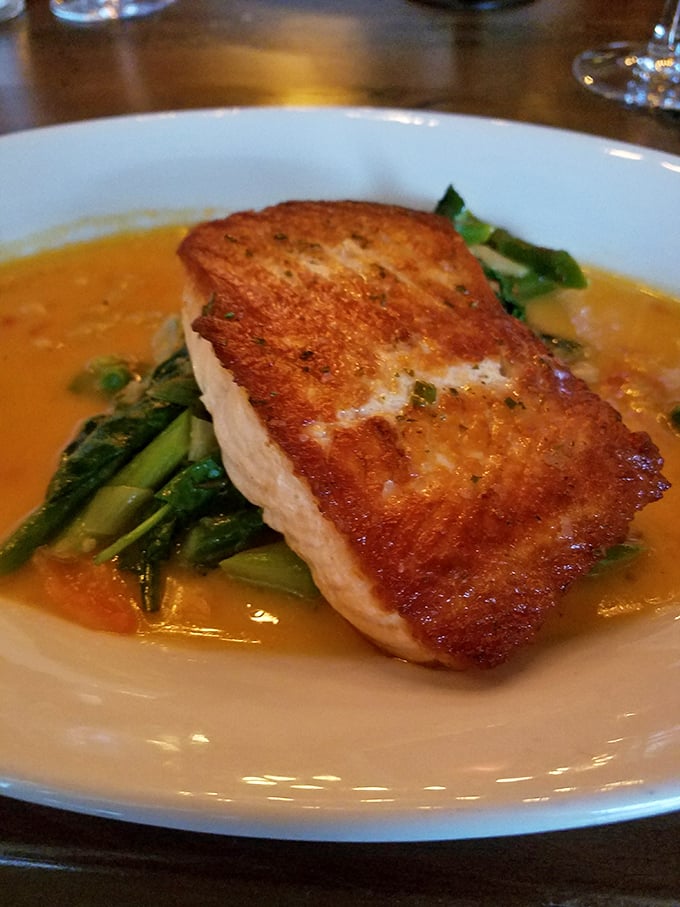 This isn't just fish—it's seafood architecture, perfectly balanced on a bed of greens with a sauce that deserves its own fan club.