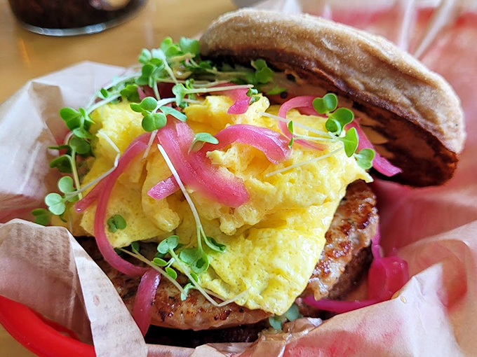 The breakfast sandwich in its natural habitat—nestled in paper, bursting with golden eggs and those magical pink pickled onions that brighten everything they touch.