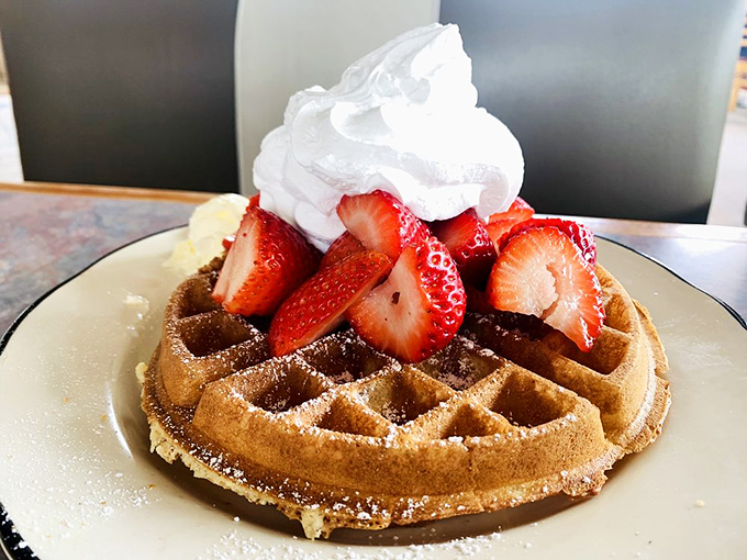 This waffle doesn't just carry strawberries—it showcases them like precious jewels, crowned with a dollop of whipped cream that's melting just so.