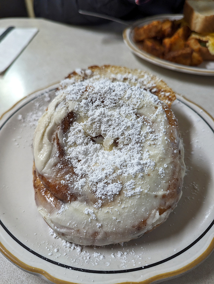The cinnamon roll arrives dusted with powdered sugar like fresh Erie snowfall—a sweet spiral of dough that's been kissed by butter and transformed by heat. 